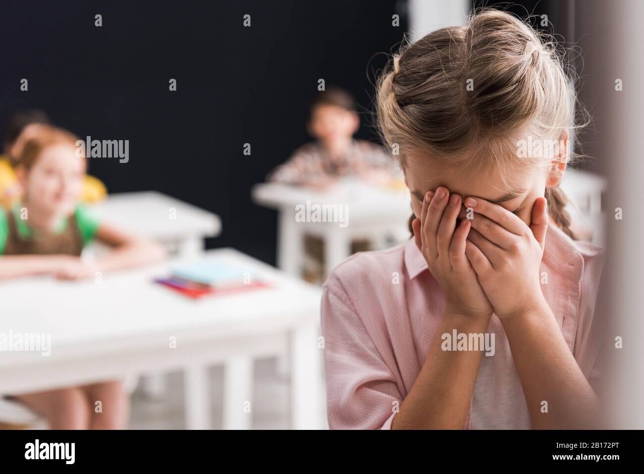 selective focus of frustrated schoolkid crying near classmates ...