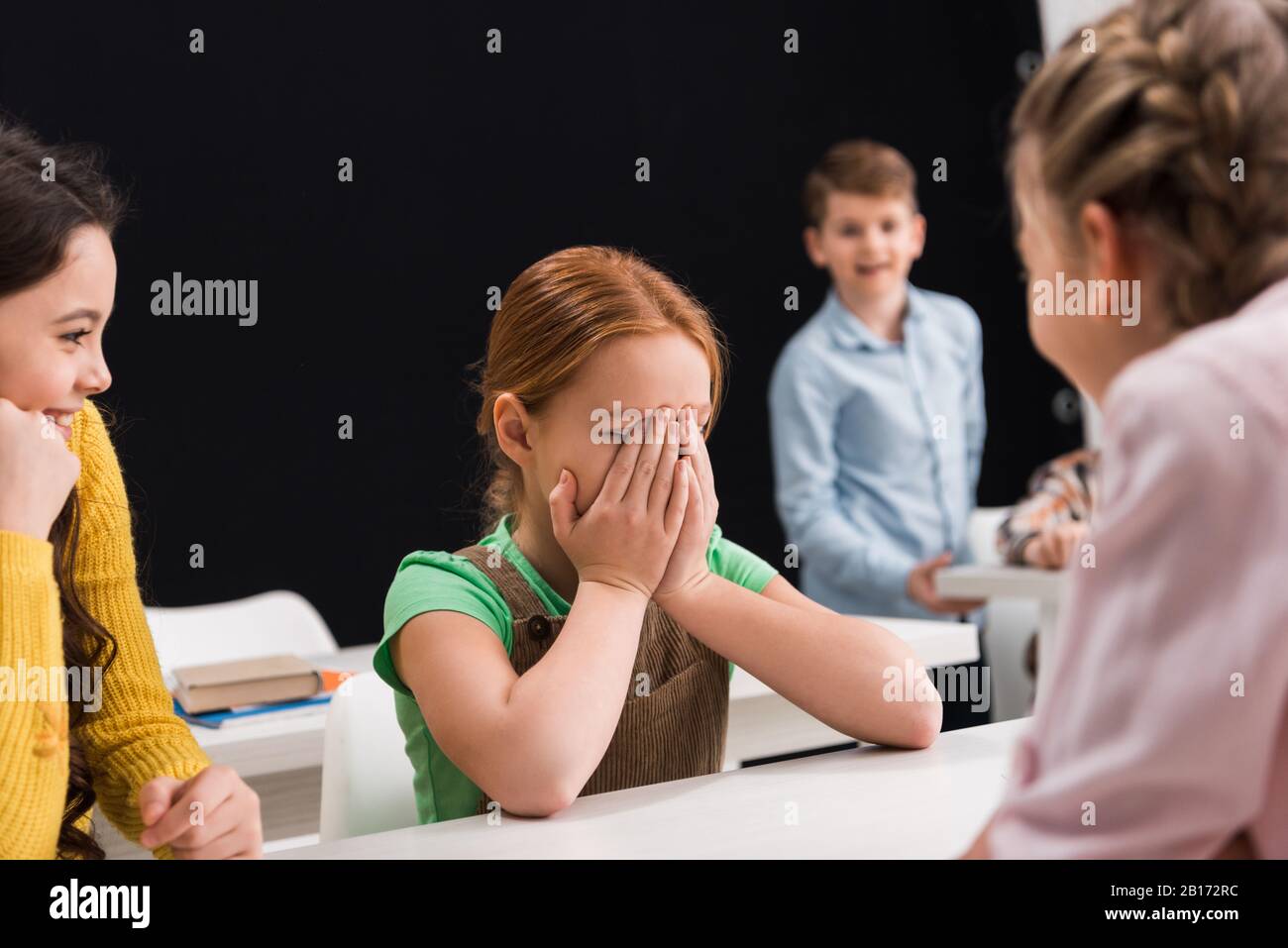 selective focus of upset kid crying near classmates on black, bullying ...