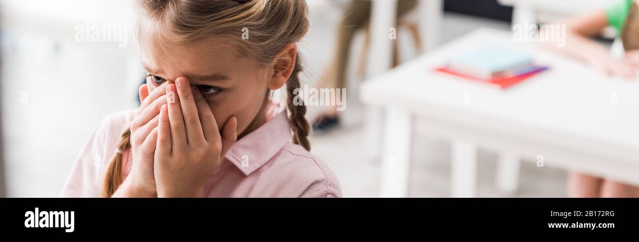 panoramic shot of upset schoolkid crying in classroom, bullying concept ...