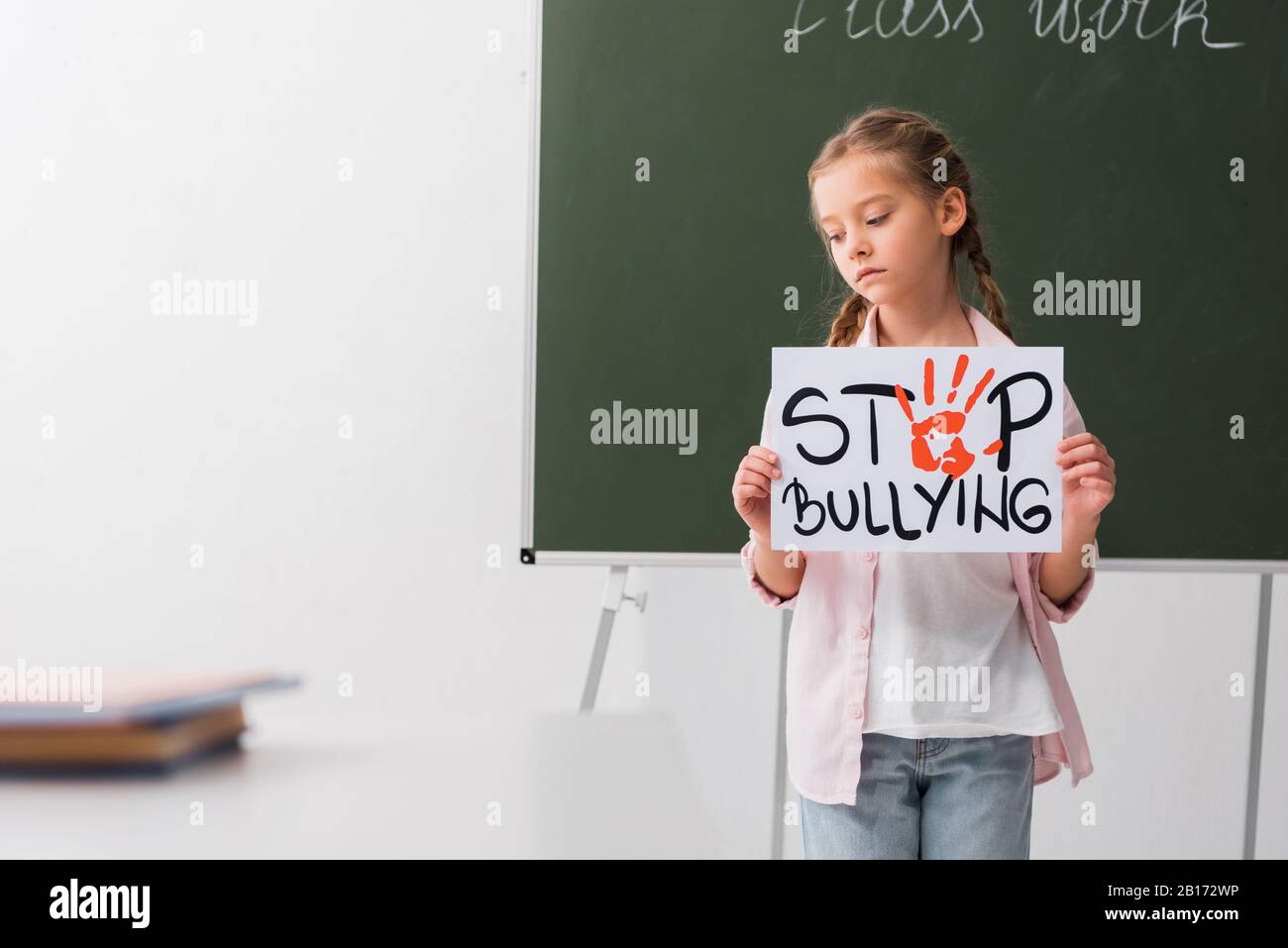 selective focus of sad schoolgirl holding placard with stop bullying ...