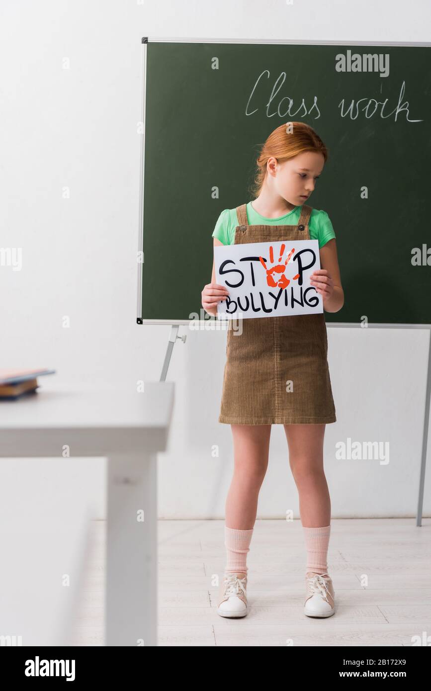 selective focus of cute schoolgirl holding placard with stop bullying ...