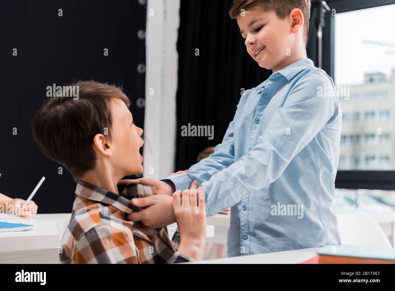 selective focus of cruel schoolkid smiling while bullying classmate ...