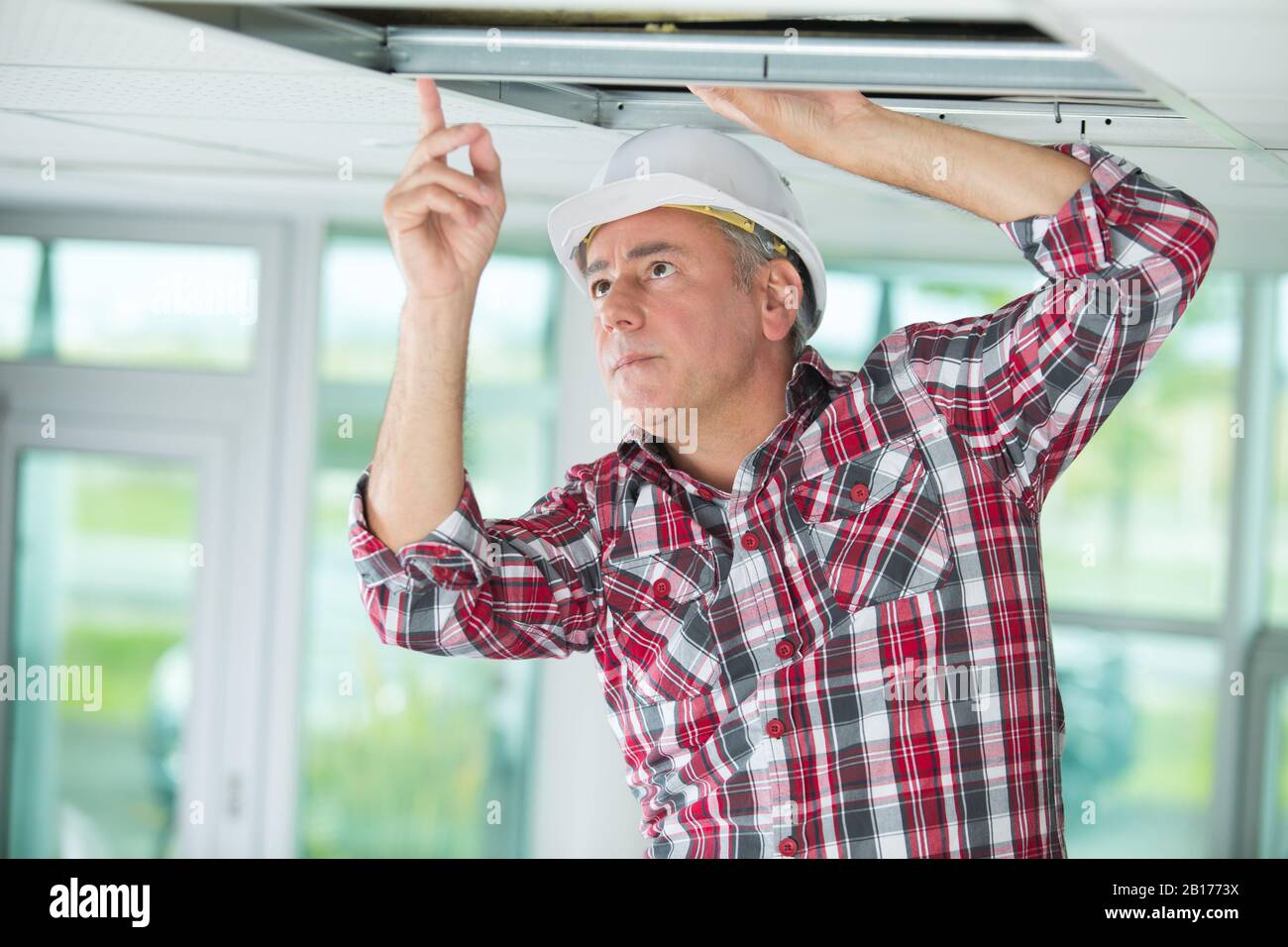 man install suspended ceiling in house Stock Photo - Alamy