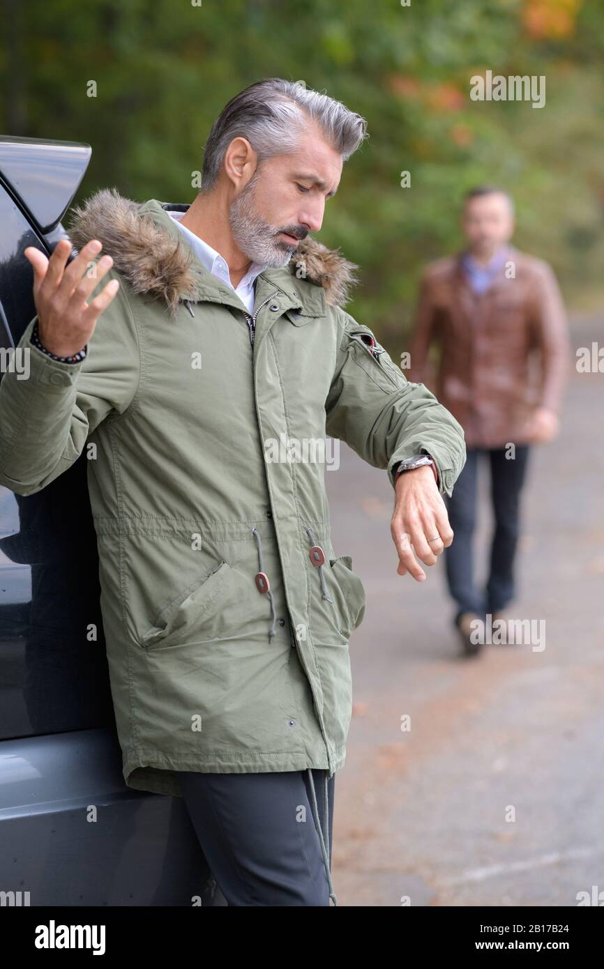 impatient man looking at watch second man approaching in background ...