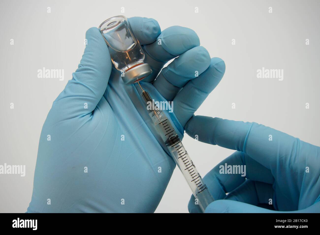 Hands in blue gloves filling a syringe from a vial Stock Photo - Alamy