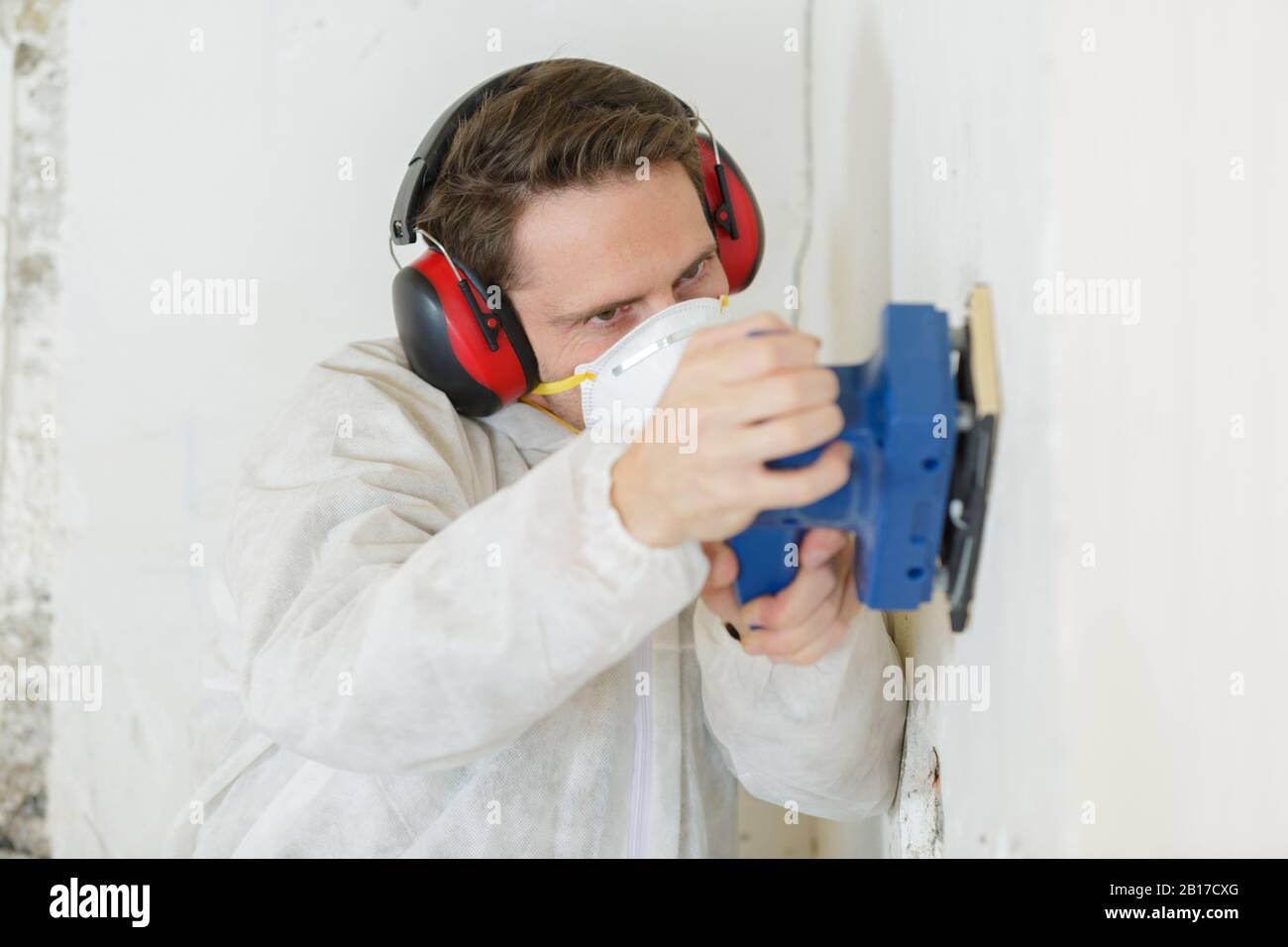 builder wearing dust mask using a sander on wall surface Stock Photo ...
