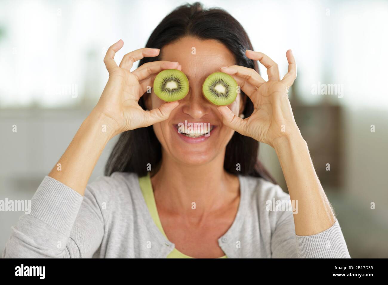 beautiful young woman holding two cut kiwis on her eyes Stock Photo - Alamy