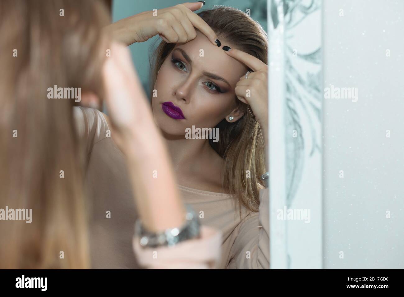 Young beautiful model with stylish makeup looking at reflection in ...