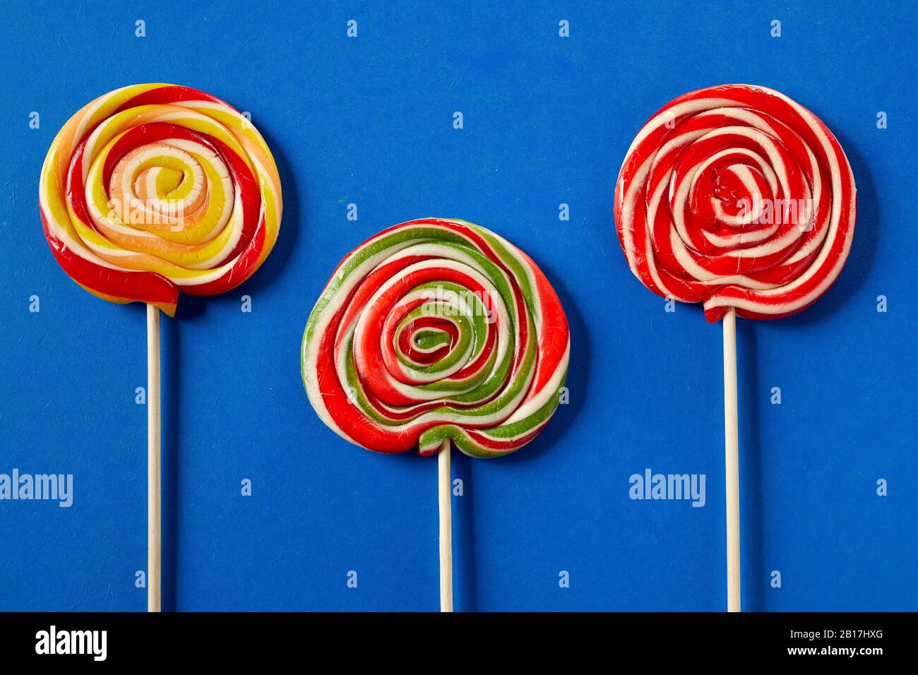 Three colorful spiral lollipops on sticks on a blue background arranged ...