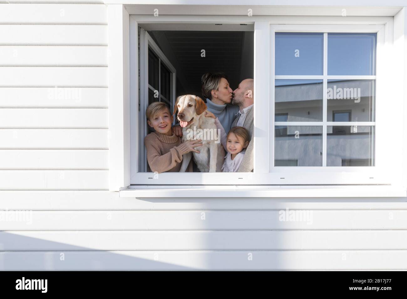 Happy family with two children and a dog at opened window of their ...