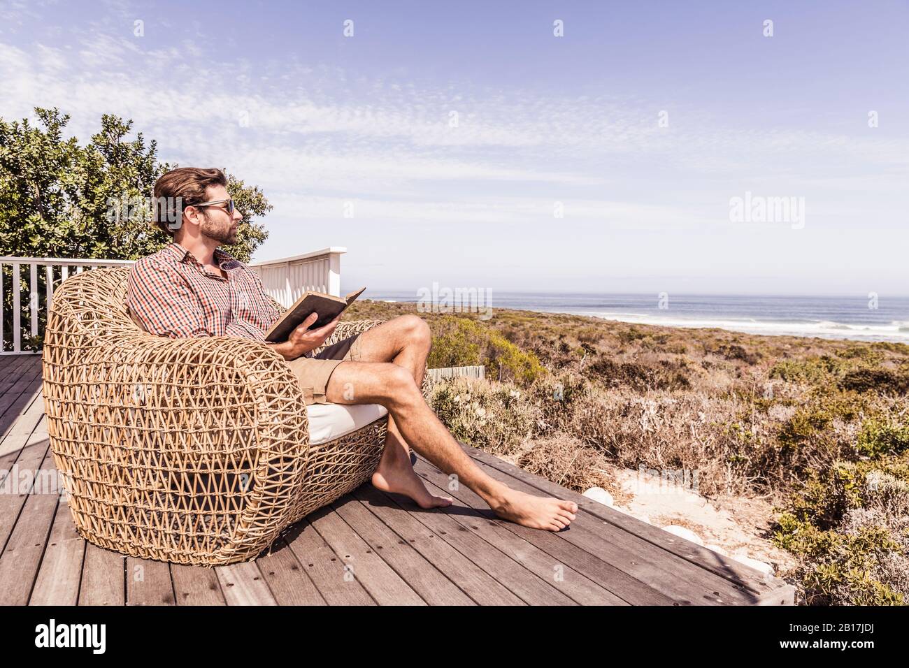 Man reading a book on a deck at the coast Stock Photo - Alamy