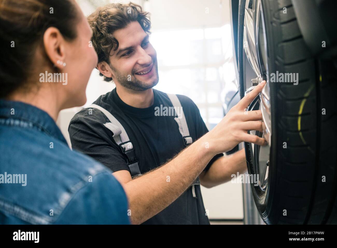 Smiling car mechanic and client looking at tire in workshop Stock Photo ...