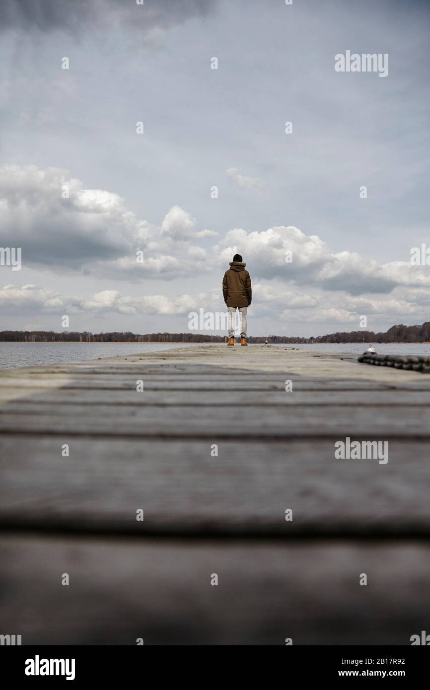 Back view of young man standing on a jetty looking at lake Stock Photo ...