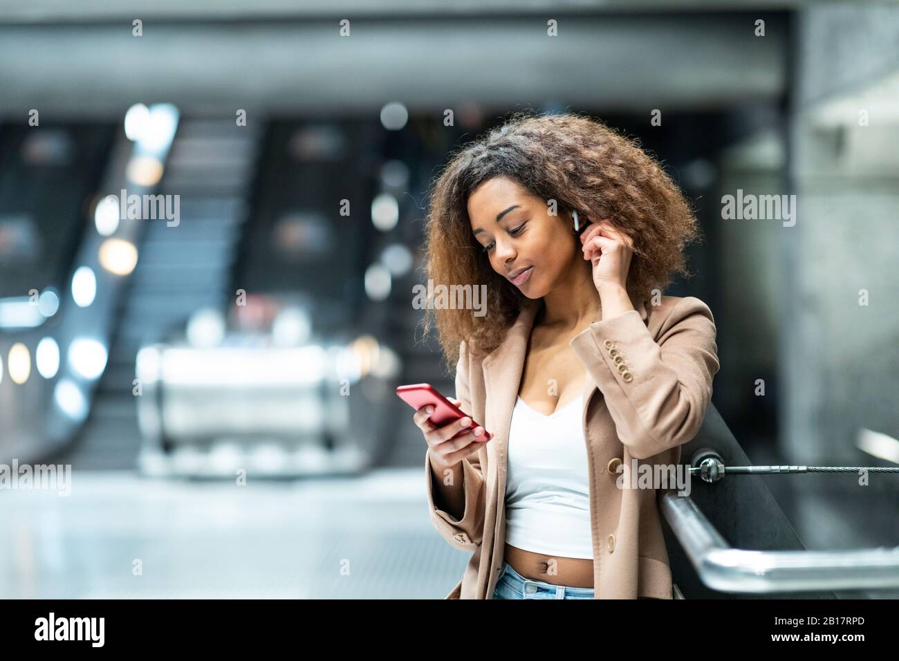Young woman with cell phone and earbuds at subway station Stock Photo ...