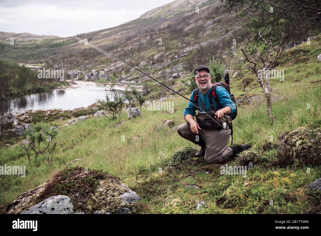 Laughing fly fisherman at river bank with mountains, Lakselv, Norway ...
