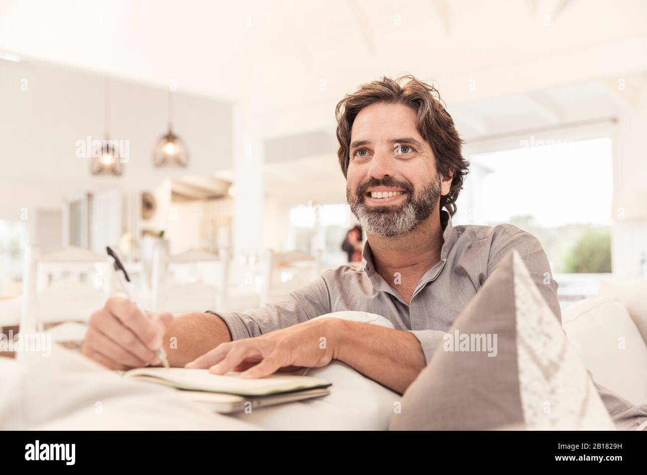 Smiling bearded man sitting on couch taking notes Stock Photo - Alamy