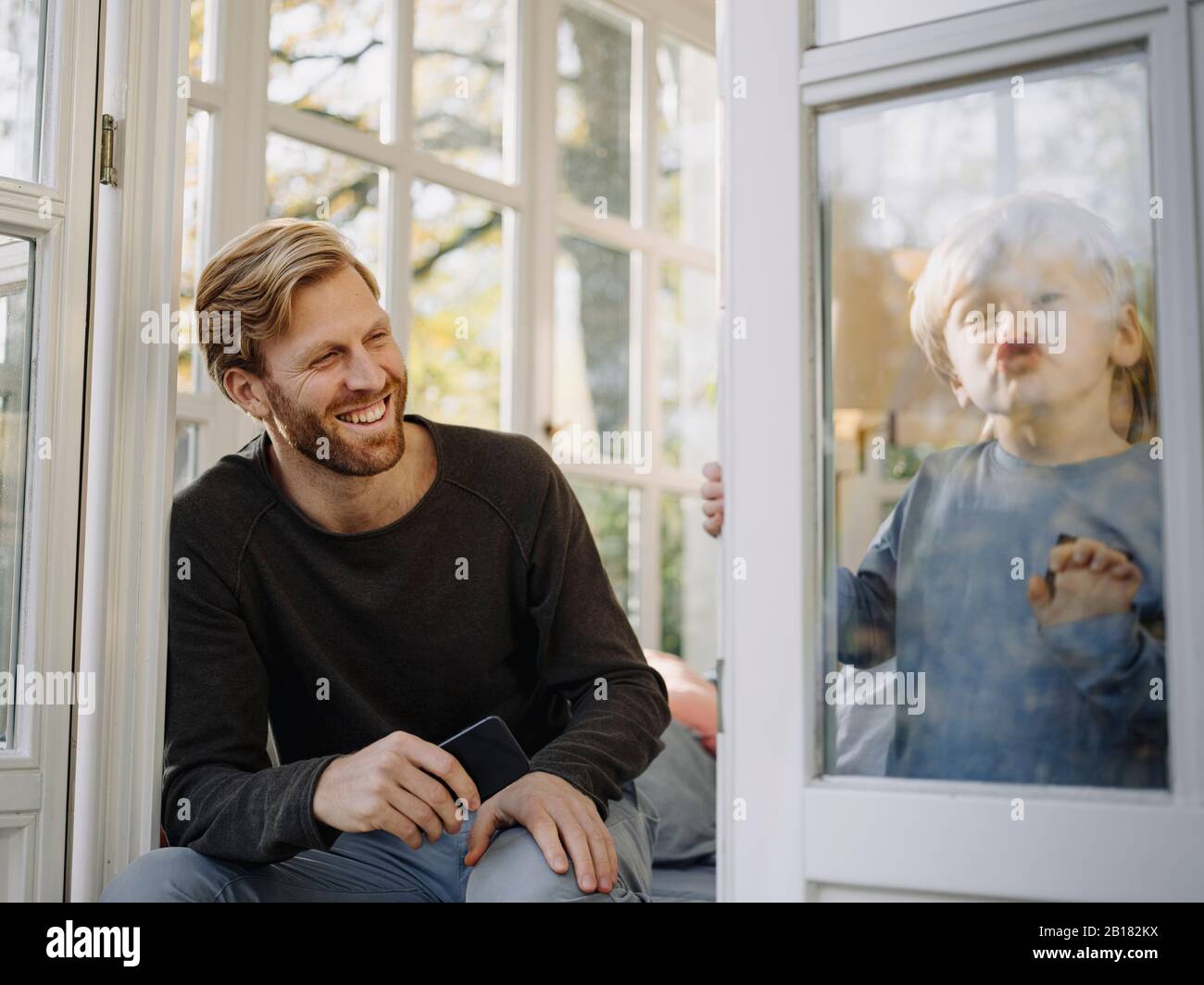 Happy father watching son grimacing at windowpane Stock Photo - Alamy