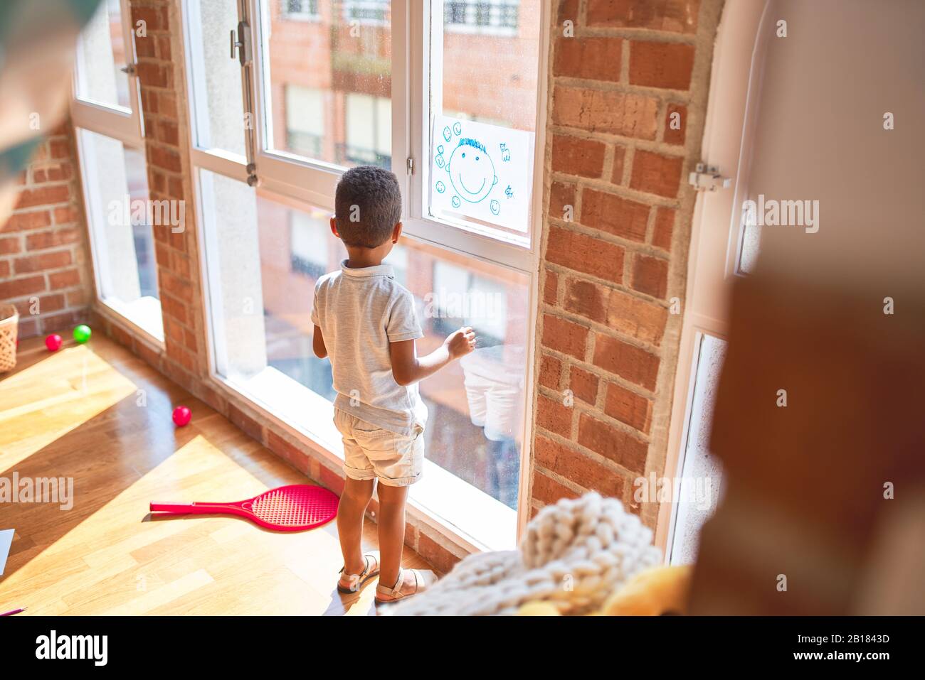 Beautiful african american toddler standing looking through the window ...