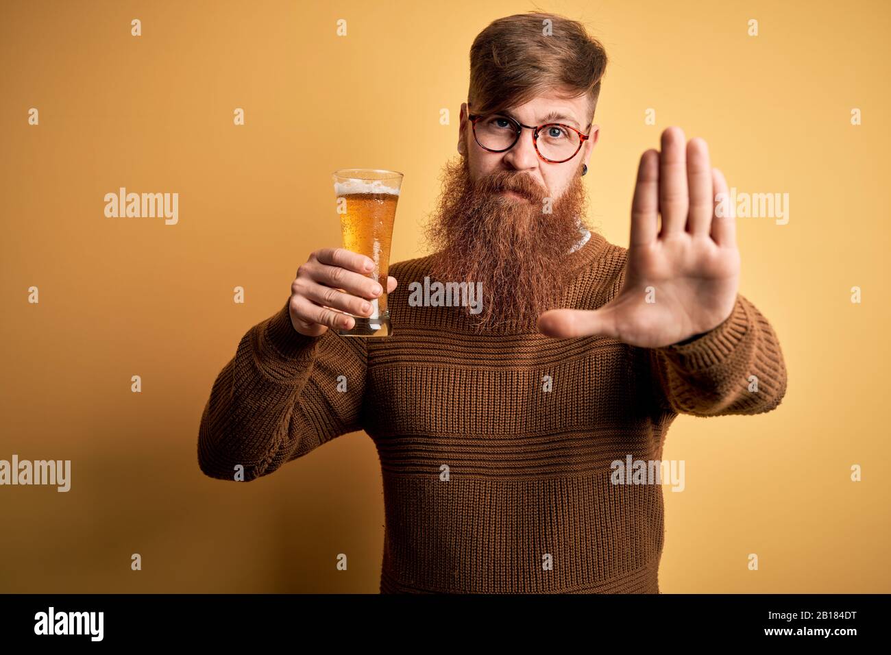 Irish redhead man with beard drinking a glass of refreshing beer over ...