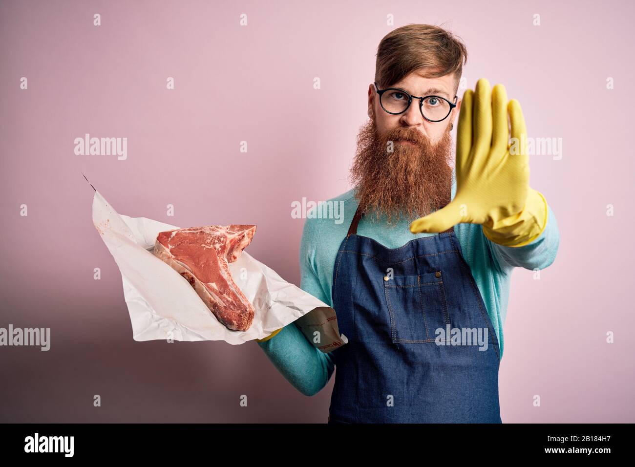 Redhead Irish butcher man with beard holding raw beef steak over pink ...