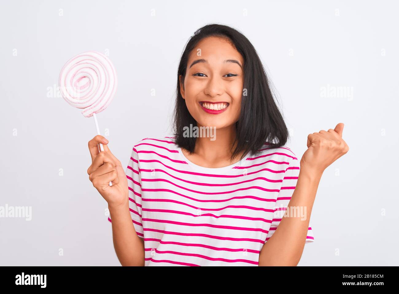 Young beautiful chinese woman eating lollipop standing over isolated ...