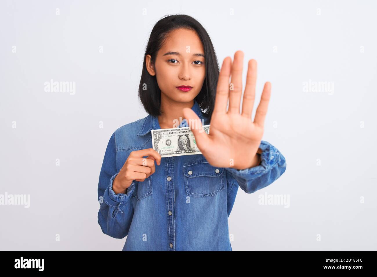 Young beautiful chinese woman holding one dollar standing over isolated ...