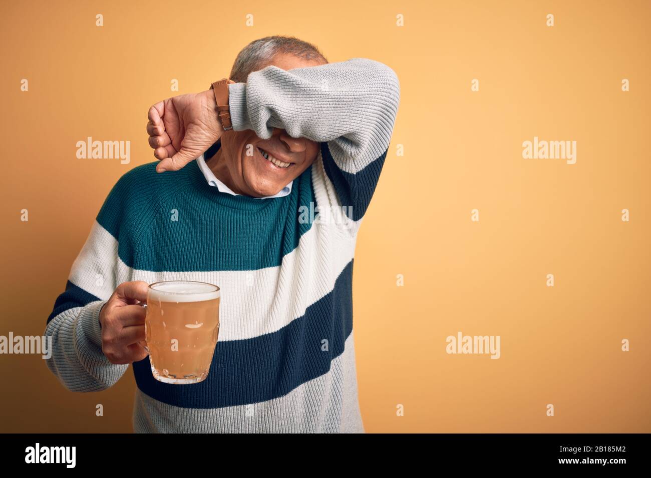 Senior handsome man drinking jar of beer standing over isolated yellow ...