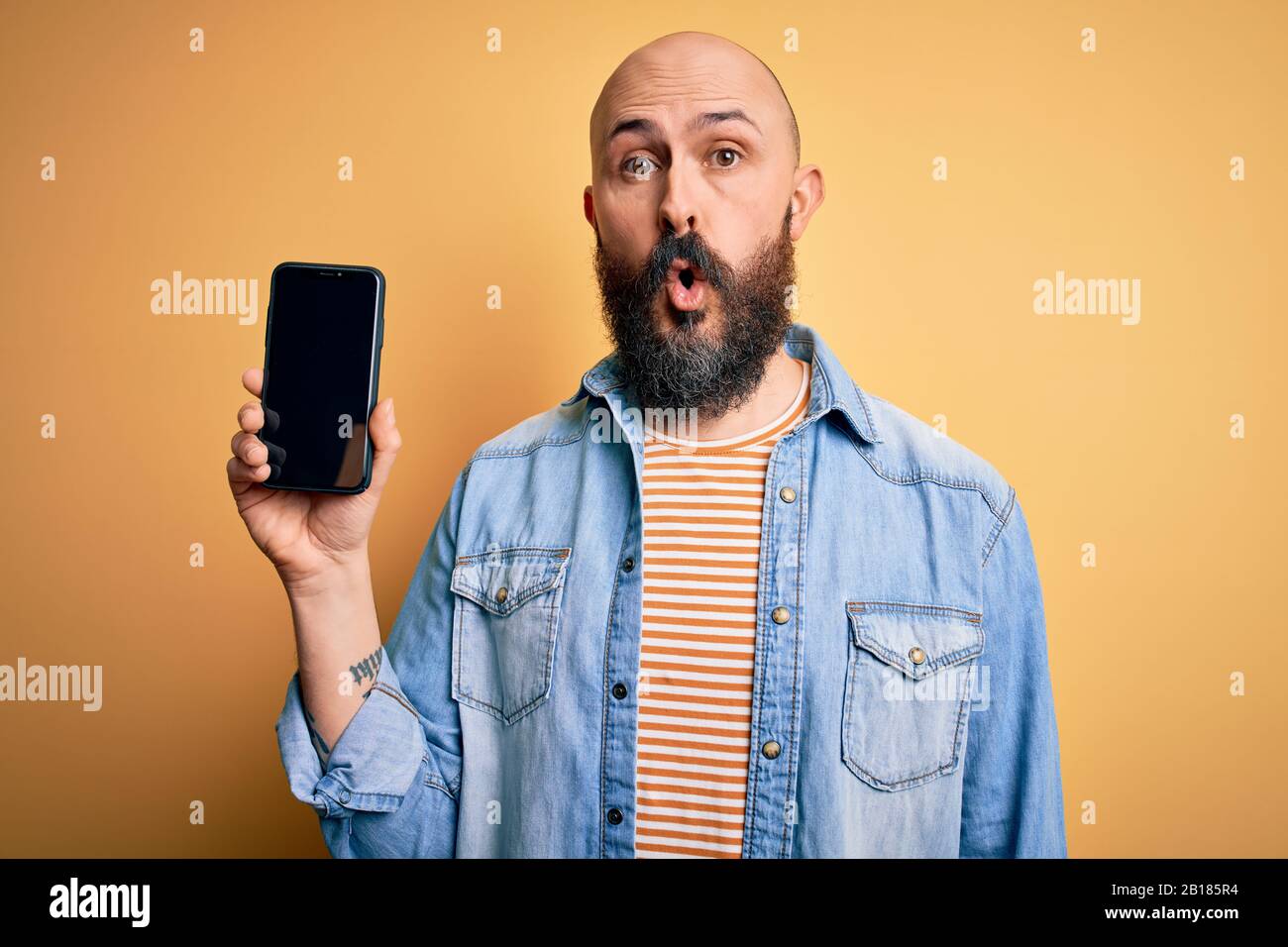 Handsome bald man with beard holding smartphone showing screen over ...