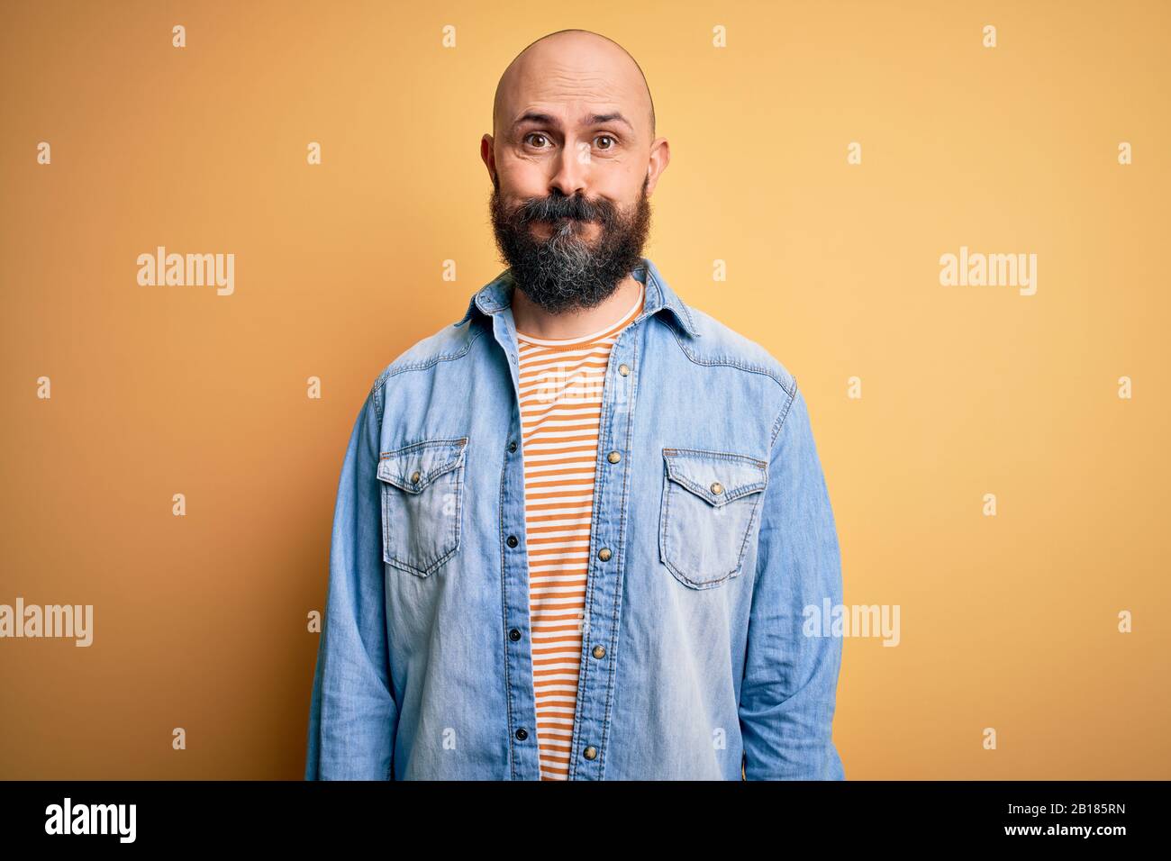 Handsome bald man with beard wearing casual denim jacket and striped t ...