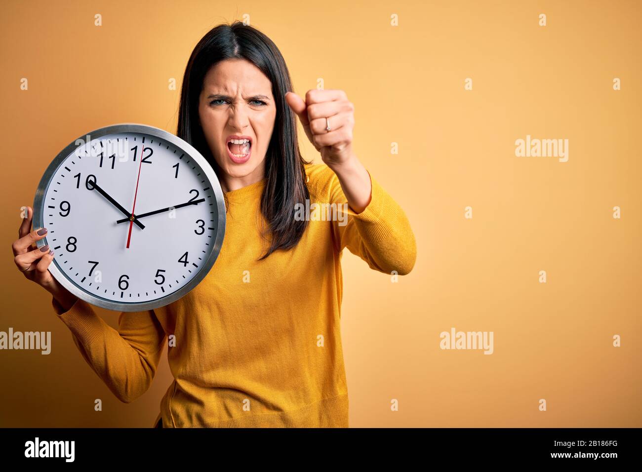 Young woman with blue eyes doing countdown holding big clock over ...