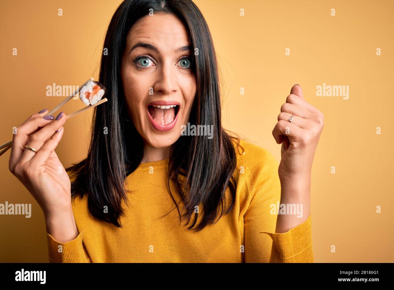 Young brunette woman with blue eyes eating salmon maki sushi using ...