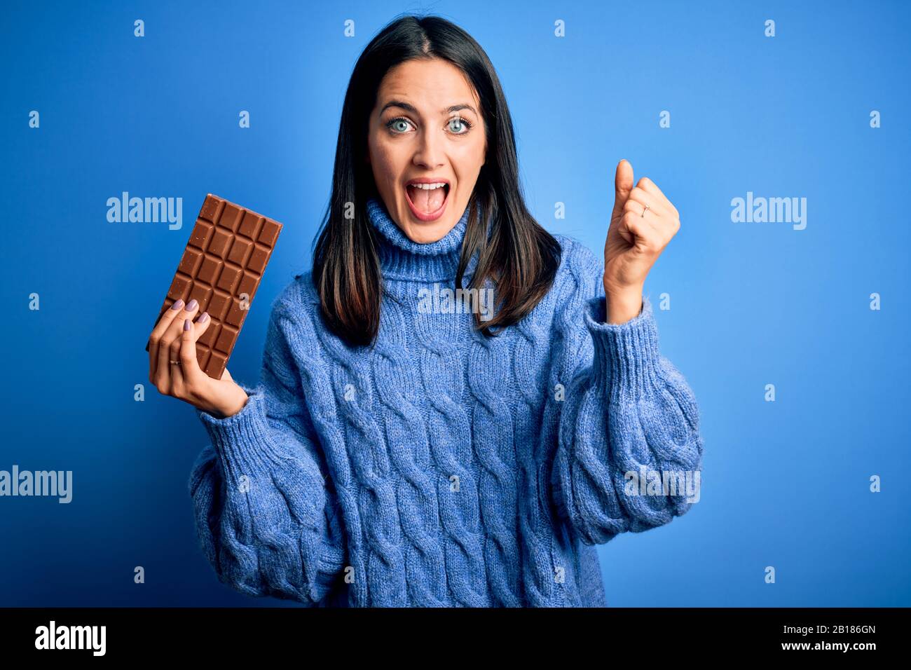 Young woman with blue eyes holding sweet chocolate bar standing over ...