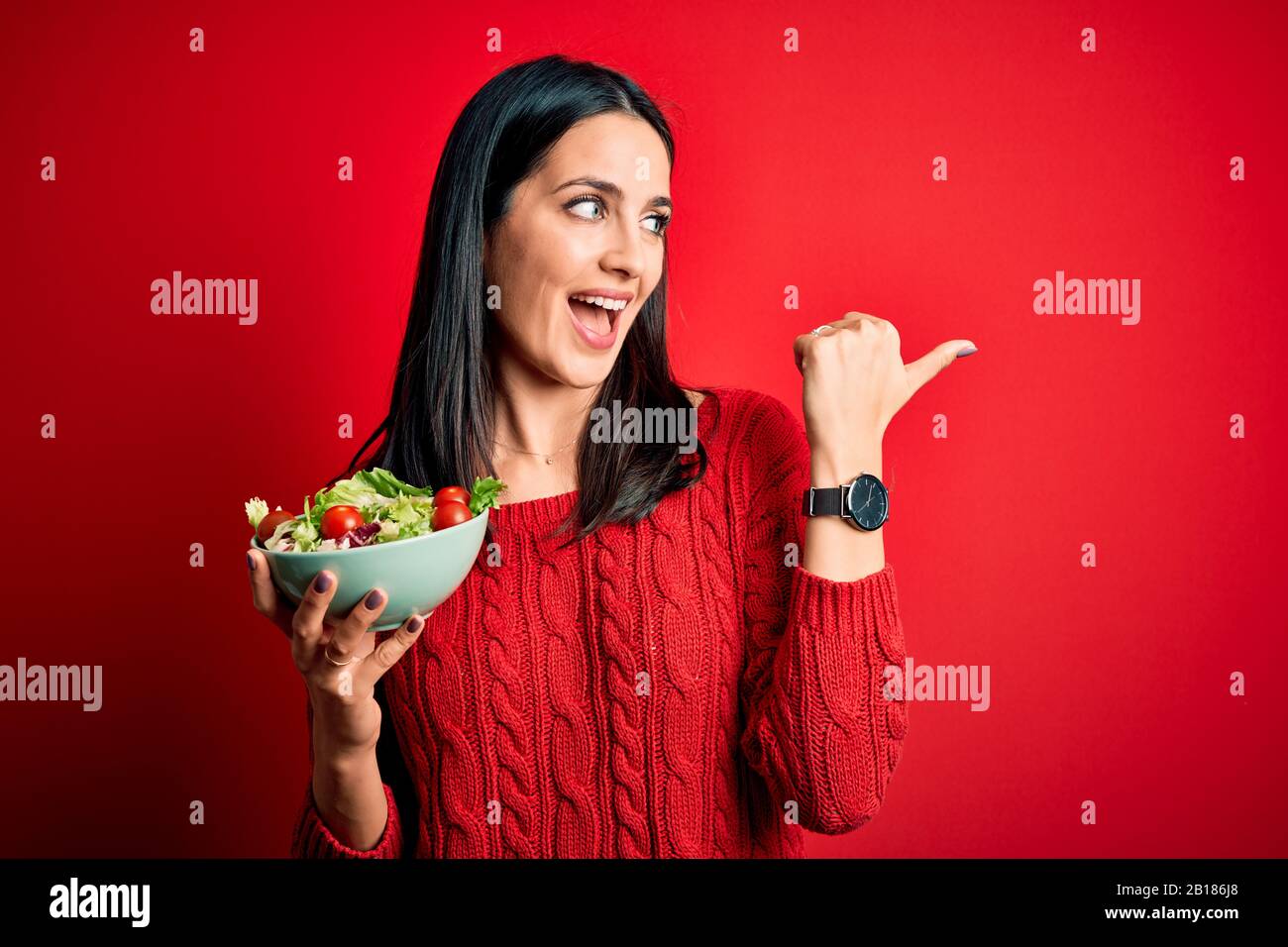 Young brunette woman with blue eyes eating healthy green salad over ...