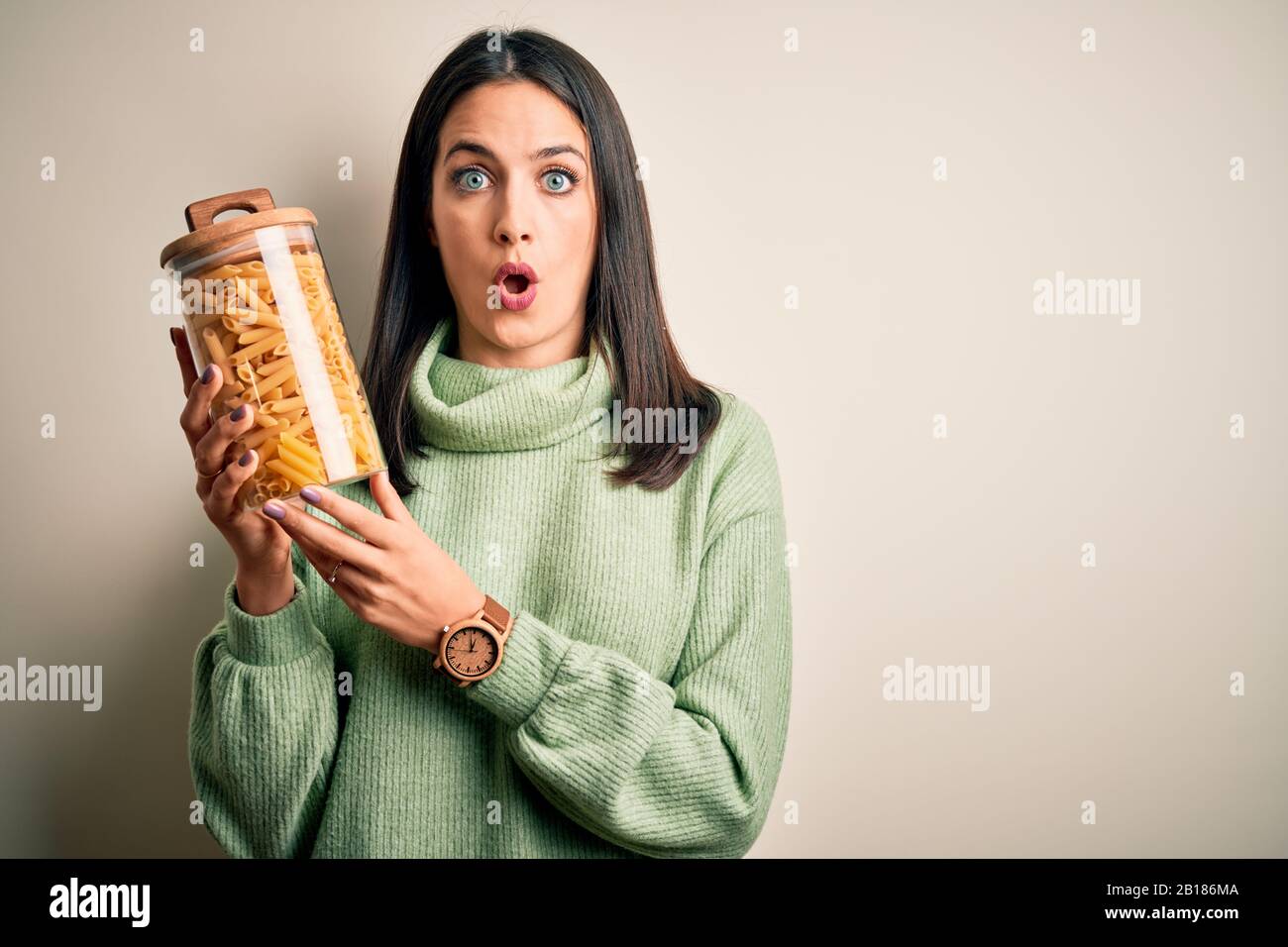 Young brunette woman holding dry italian macaroni over brown isolated ...