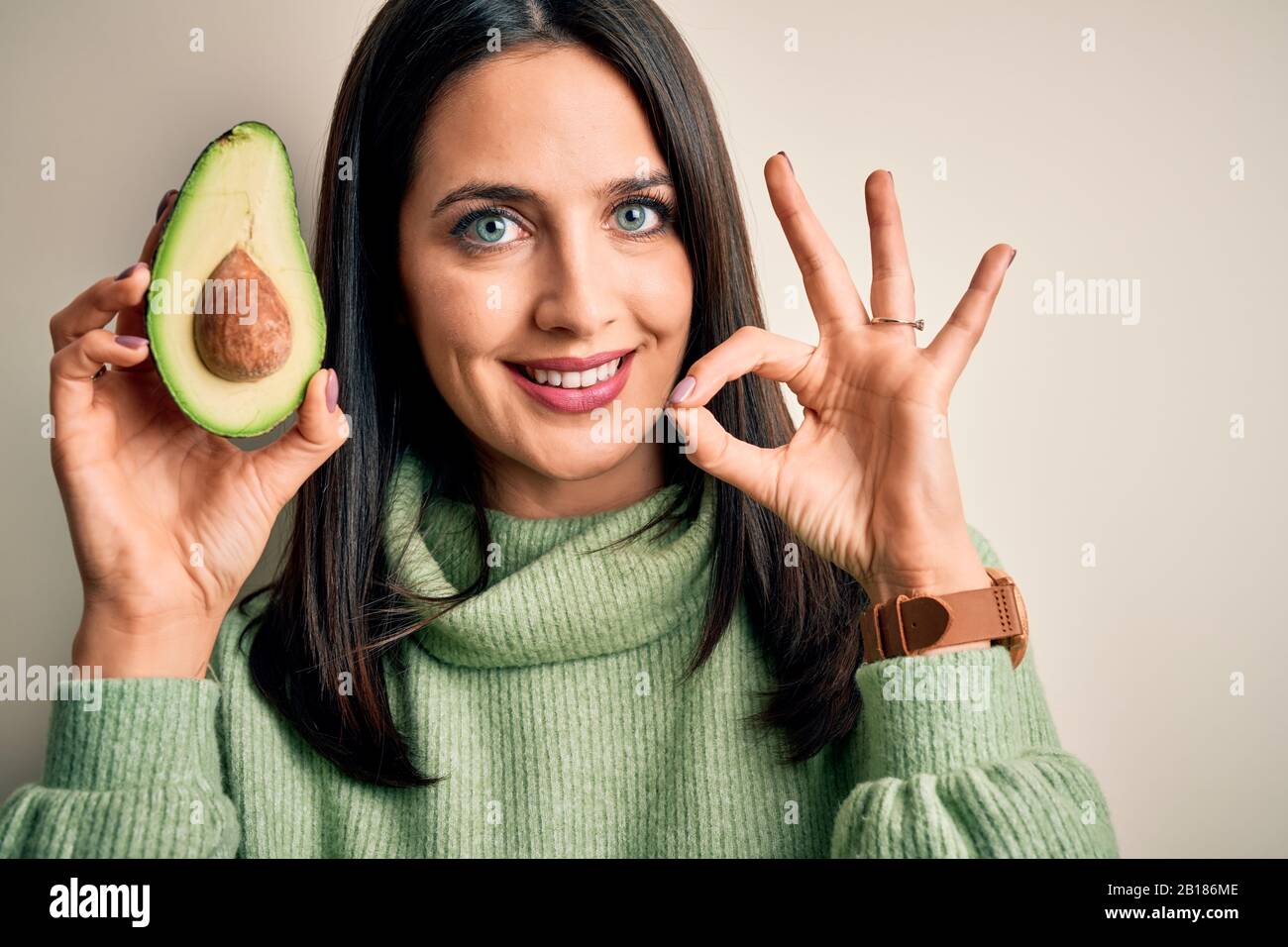 Young woman with blue eyes holding middle healthy avocado over isolated ...