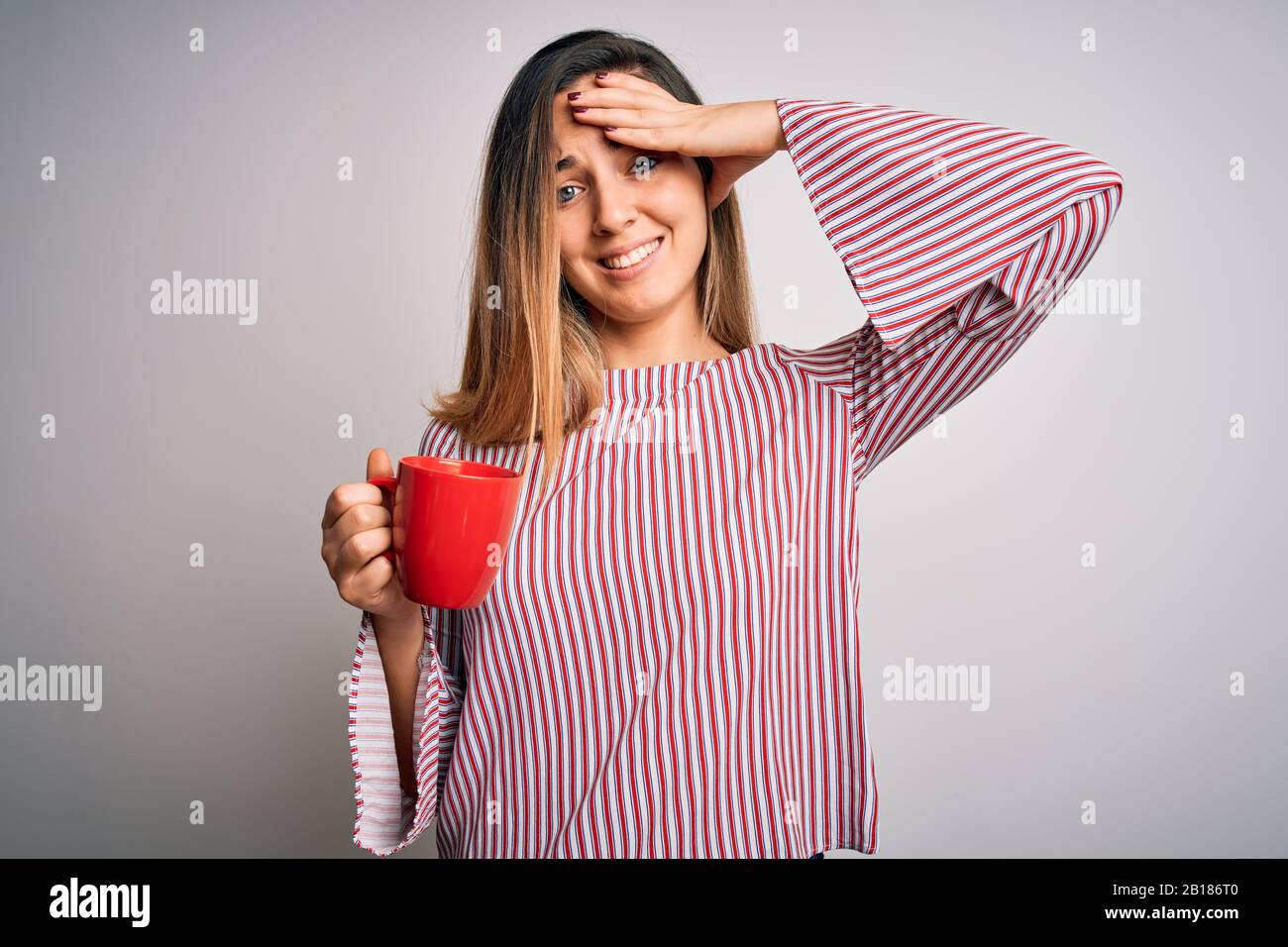 Beautiful blonde woman with blue eyes drinking red mug of coffee over ...