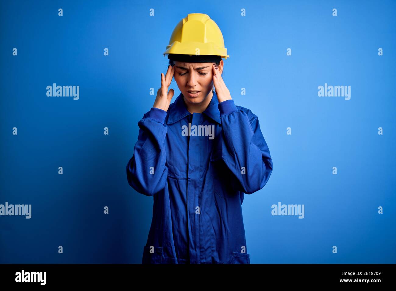 Young beautiful worker woman with blue eyes wearing security helmet and ...