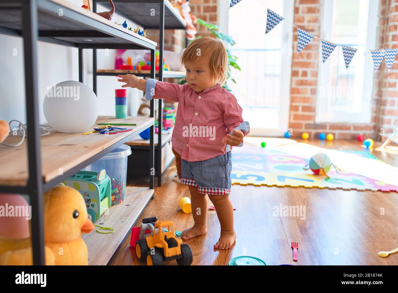 Adorable toddler playing around lots of toys at kindergarten Stock ...