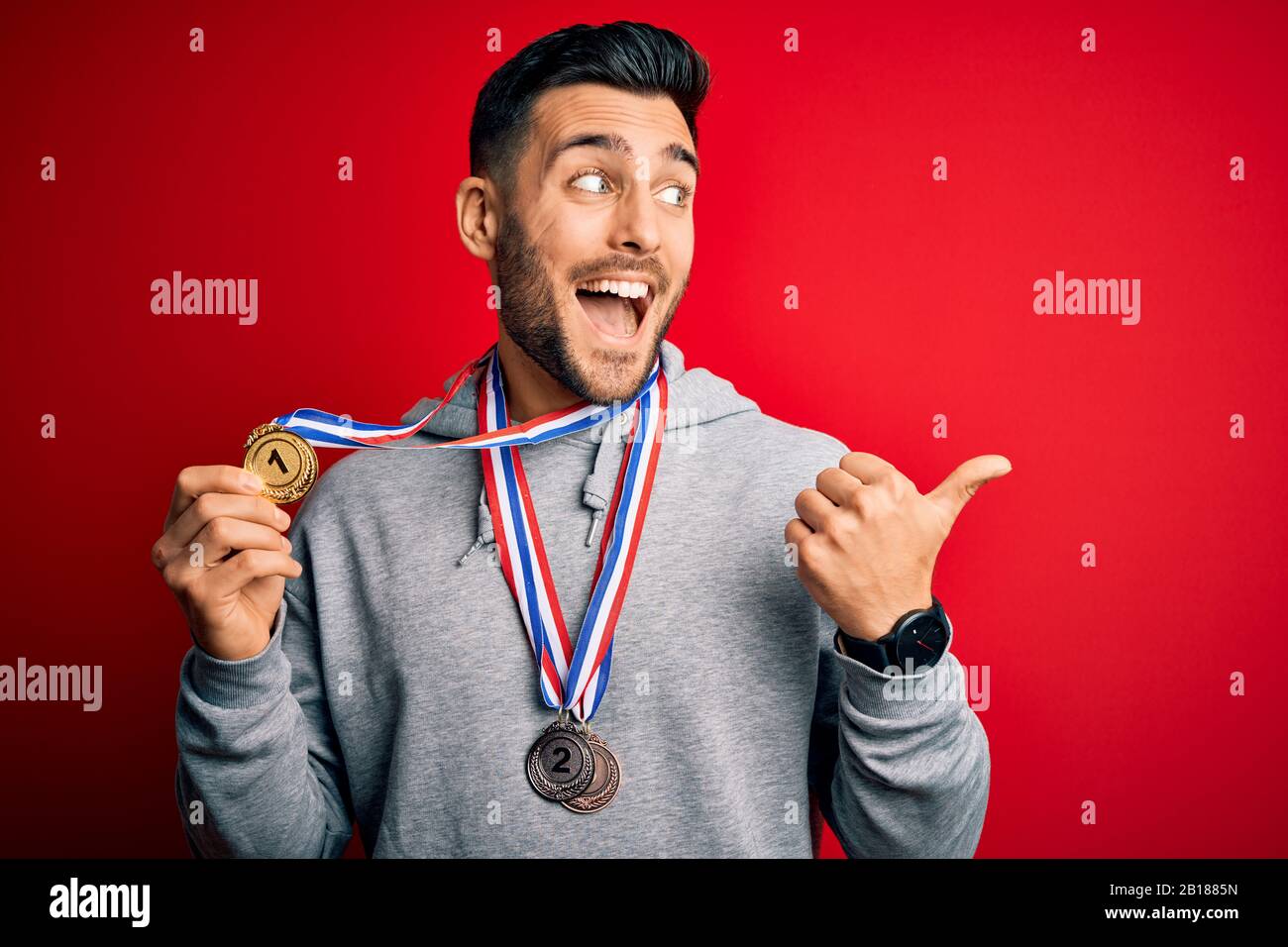 Young handsome succesful man winning medals standing over isolated red ...