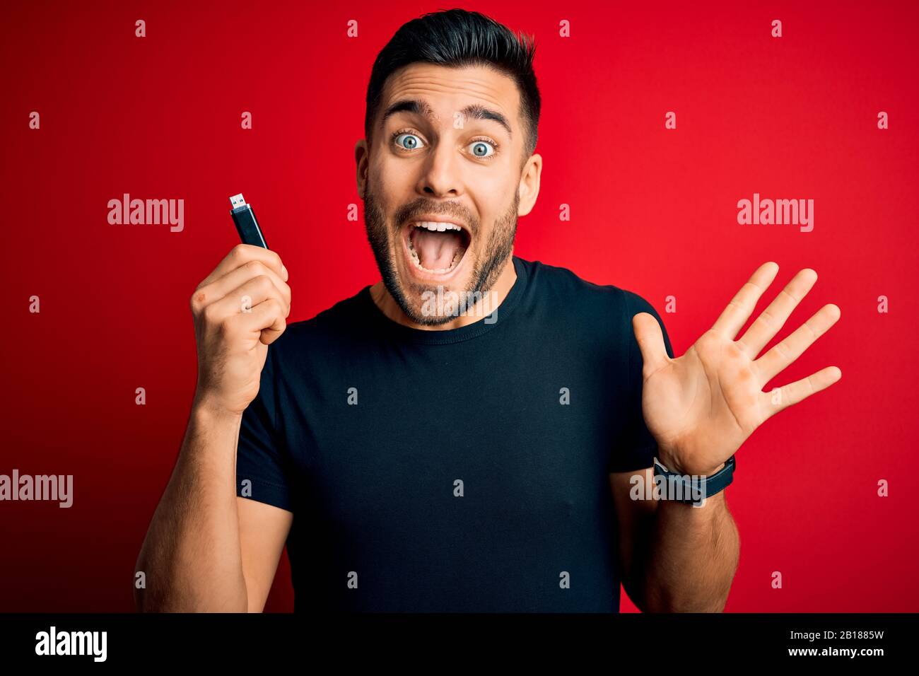 Young man holding USB memory data drive over red isolated background ...