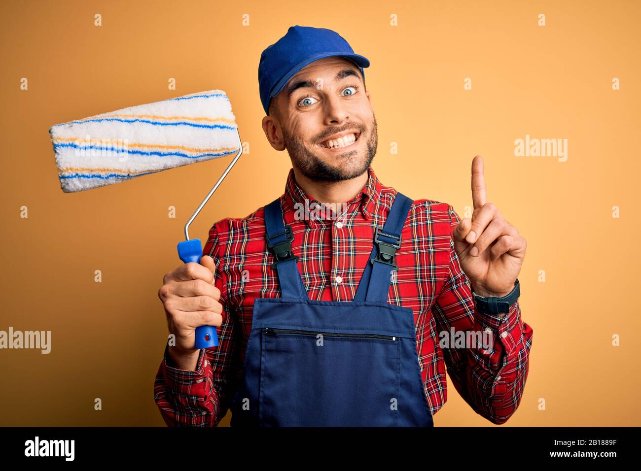 Young handsome painter man painting wall using roller over isolated ...