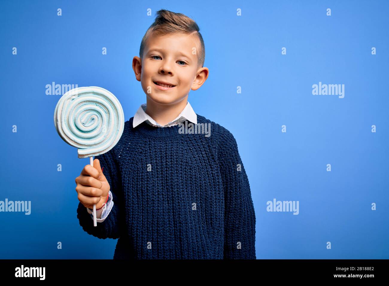 Young little caucasian kid eating sweet candy lollipop over blue ...
