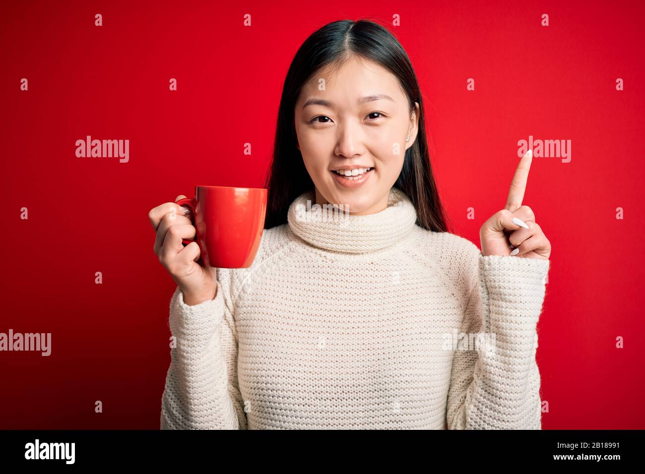 Young asian woman drinking a cup of hot coffee over isolated red ...
