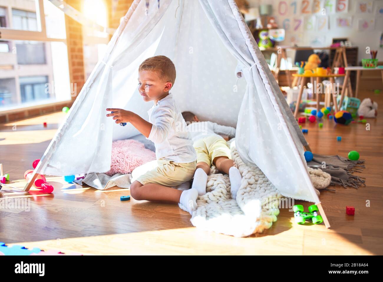 Adorable blonde twins playing inside tipi around lots of toys at ...