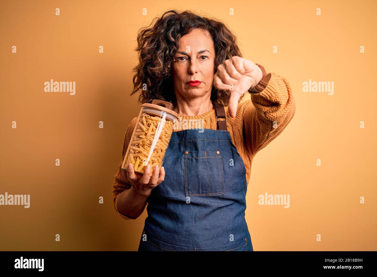 Middle age beautiful woman holding jar with macaroni pasta over ...