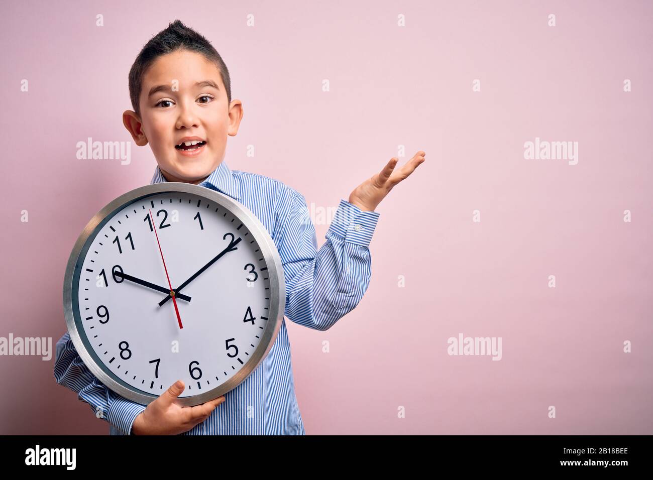 Young little boy kid holding big minute clock over isolated pink ...
