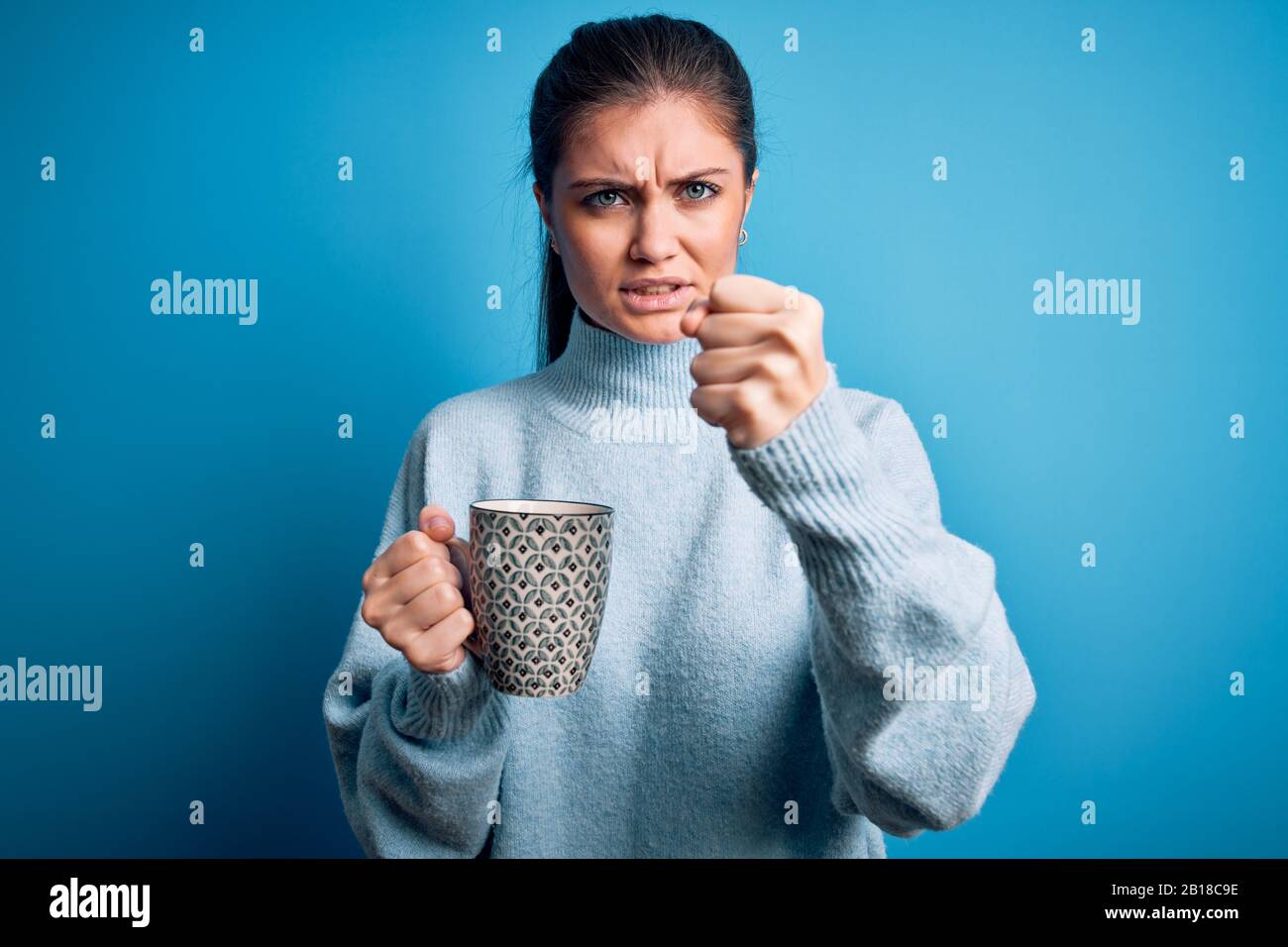 Young beautiful woman with blue eyes drinking mug of coffee over ...