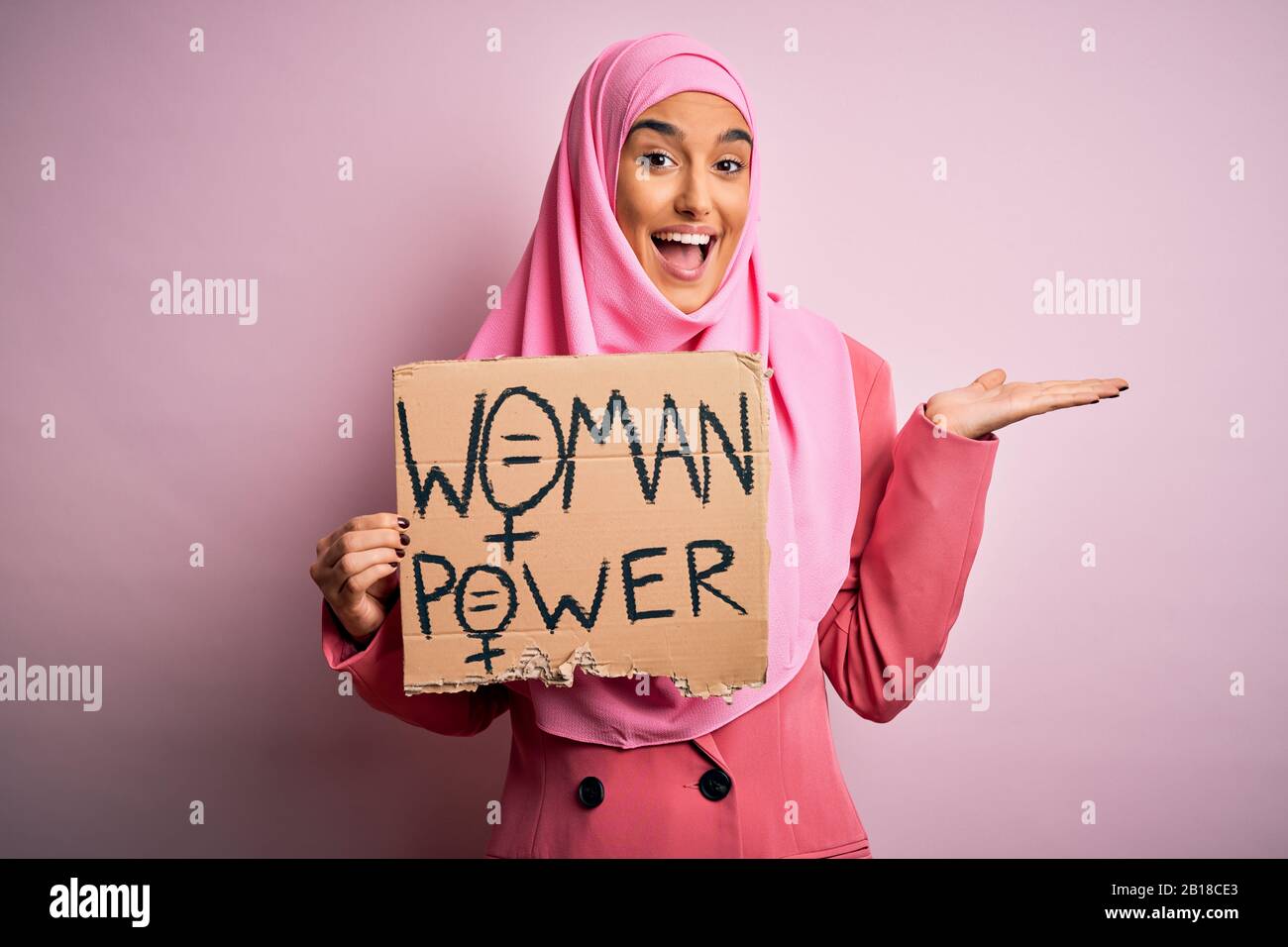 Young activist arab woman wearing pink muslim hijab holding banner with ...