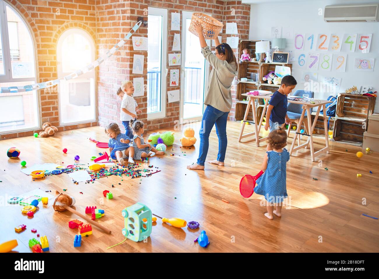 Beautiful teacher and group of toddlers playing around lots of toys at ...