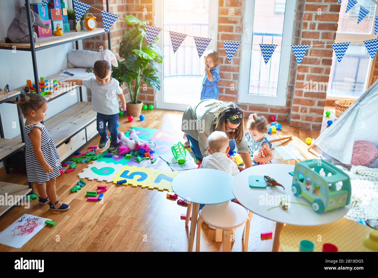 Beautiful teacher and group of toddlers playing around lots of toys at ...
